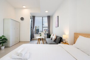 Quarto de hotel moderno com cama, sofá, mesa de jantar e vista da cidade por grandes janelas.