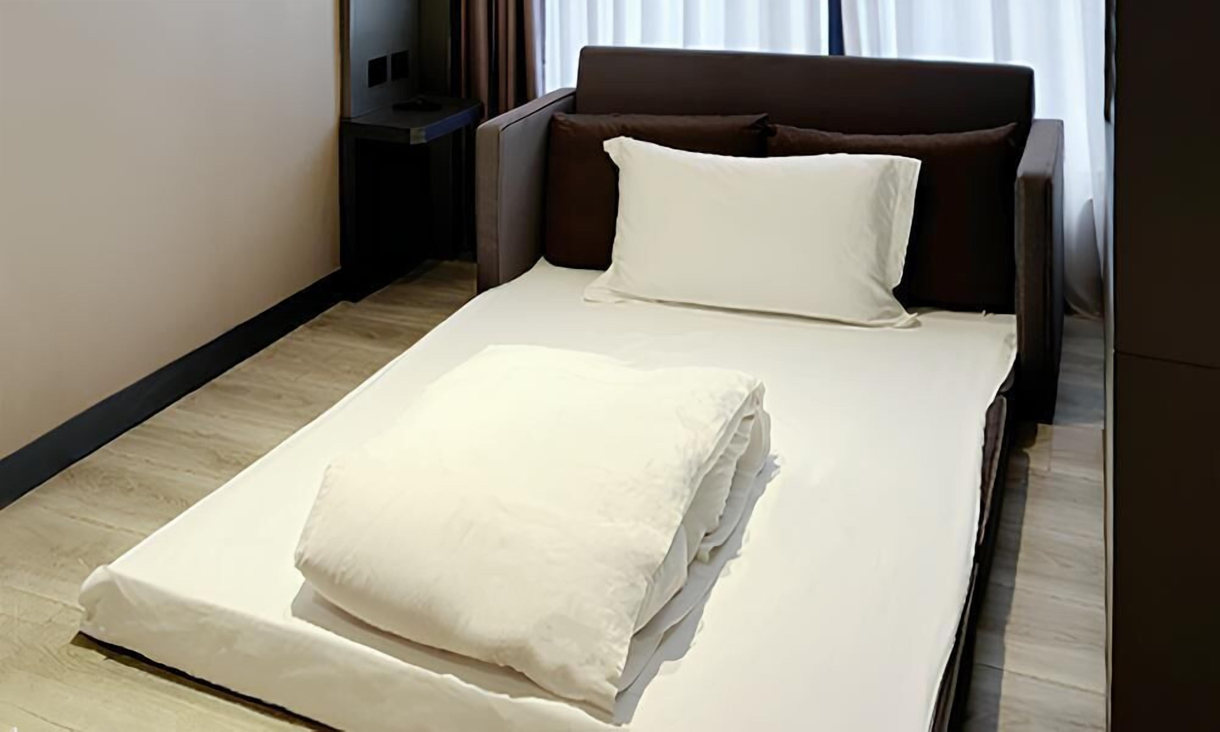 Cama bem arrumada com lençóis e almofadas brancos em quarto de hotel com piso de madeira e cabeceira marrom escura.