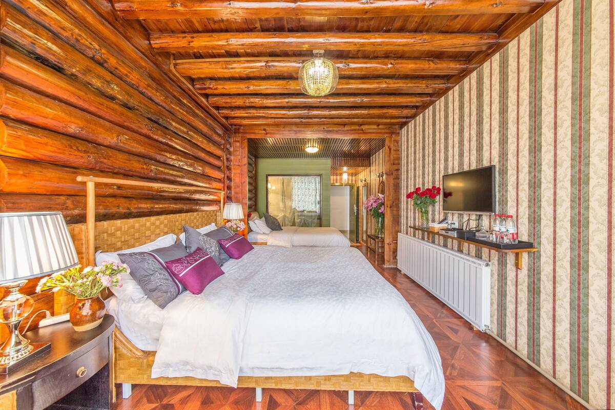 Um quarto estilo cabana de tronco com uma cama grande, teto de madeira e uma televisão numa prateleira.