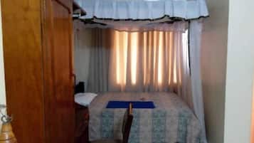 Quarto pequeno com cama de solteiro, porta de madeira, cama com colcha azul e uma cadeira.