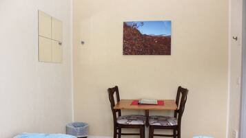 Quarto com duas camas, uma mesa de madeira com cadeiras, um quadro na parede e uma lixeira.