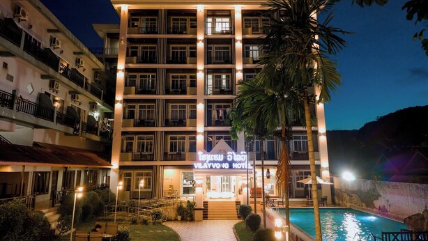Um hotel com vários andares, piscina, área de estar externa e entrada bem iluminada.