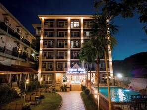 Um hotel com vários andares, piscina, área de estar externa e entrada bem iluminada.