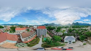 Vista aérea de uma cidade com um edifício imponente de vários andares e telhado vermelho, rodeado por edifícios menores e vegetação.