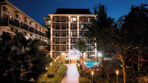 Um hotel com vários andares, piscina, área de estar externa e entrada bem iluminada.