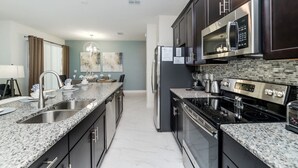 Cozinha moderna com bancadas de granito, eletrodomésticos de aço inoxidável e armários escuros.