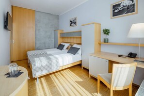 Quarto com cama, escrivaninha, cadeira e televisão.