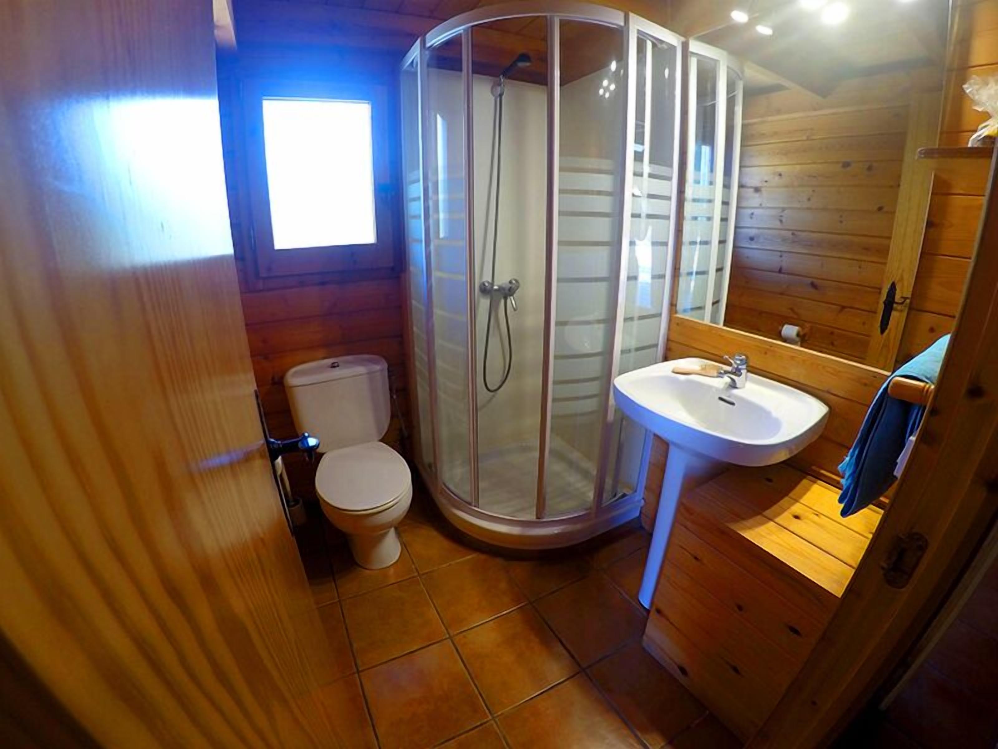 Casa de banho de uma cabana de madeira, com sanita, cabine de duche em vidro e lavatório.