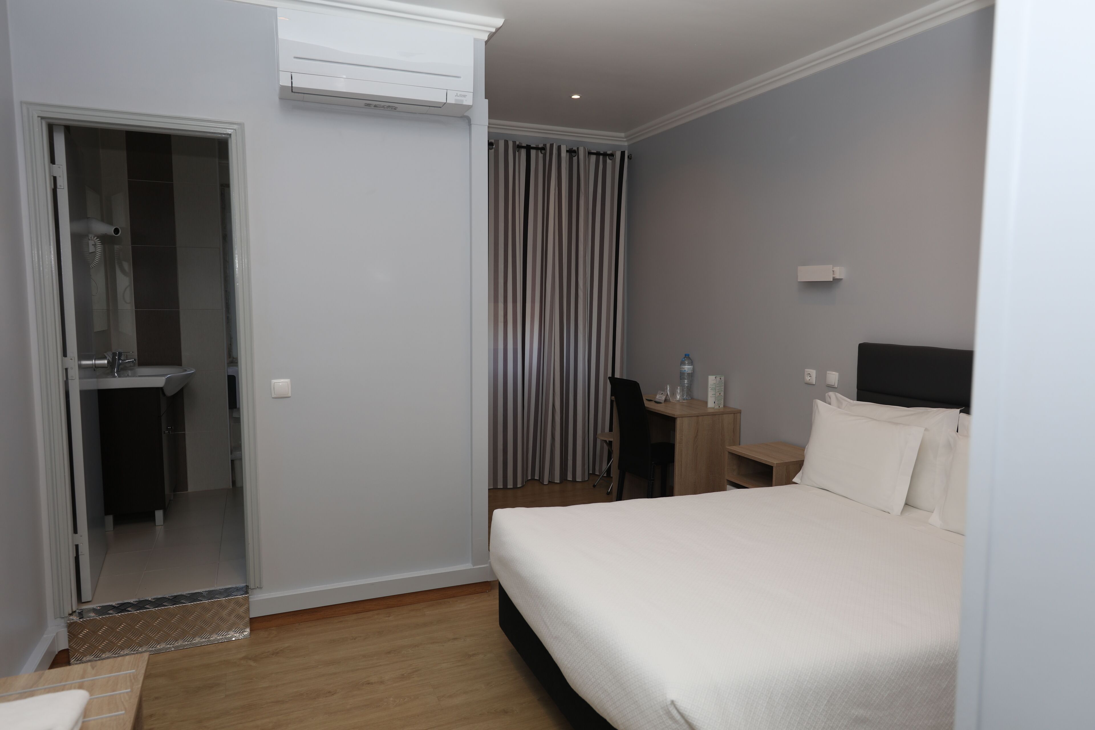 Quarto de hotel com cama, escrivaninha, cadeira, mesinha de centro e área de chuveiro.