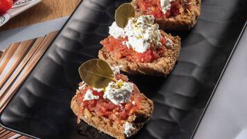 Uma placa preta retangular com três bruschettas cobertas de tomate, queijo e folhas de louro.
