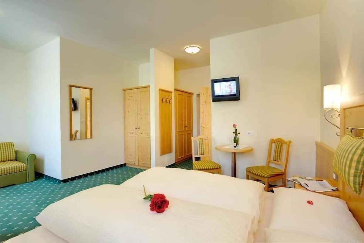 Quarto de hotel com cama, duas cadeiras, uma mesinha, espelho e televisão na parede.