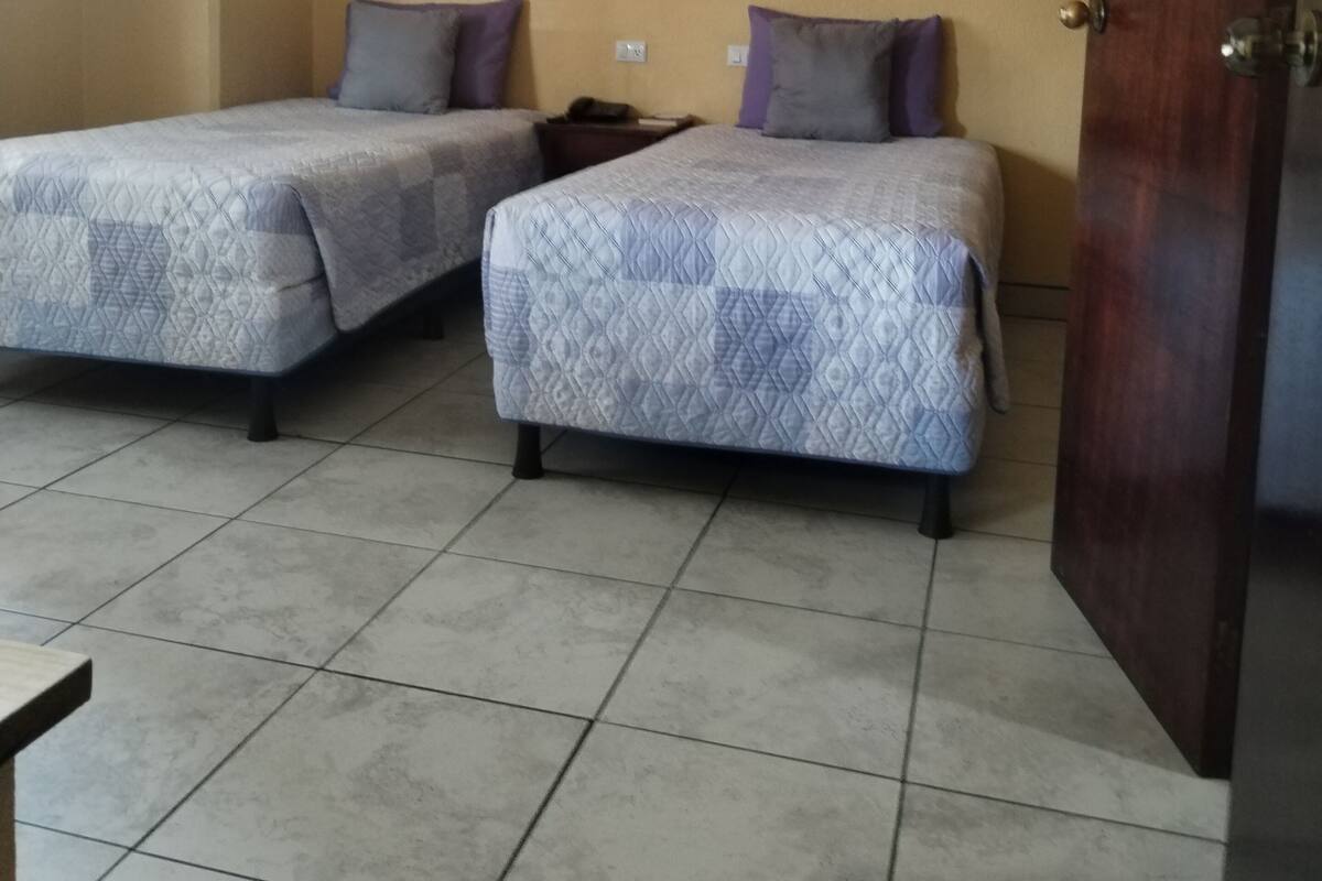 Quarto com duas camas, cada uma com colcha estampada, um quadro na parede e uma porta à direita.