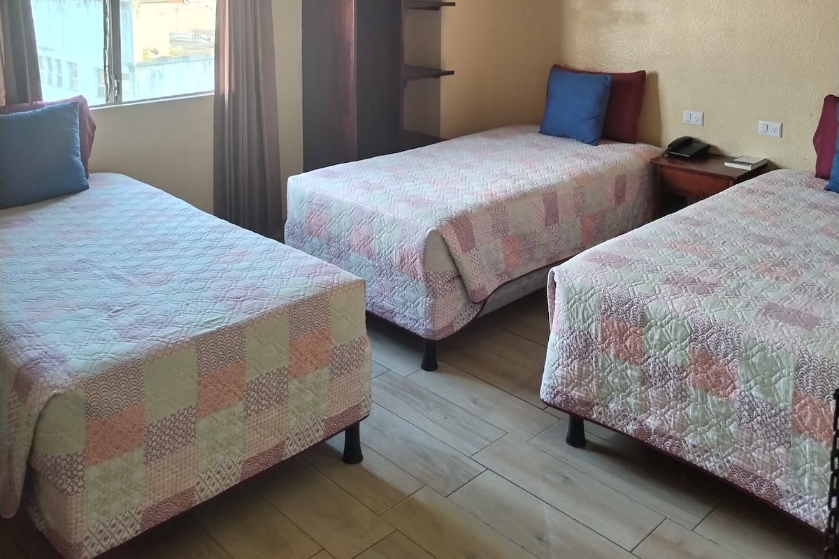 Quarto de hotel com duas camas, um guarda-roupa, uma mesa de cabeceira e uma janela com cortinas.