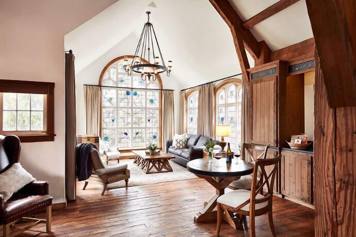 Um quarto espaçoso com assoalho de madeira, um lustre e grandes janelas com vitrais.