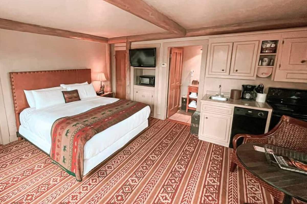 Quarto de hotel com cama, uma pequena mesa, televisão, micro-ondas e cozinha compacta.