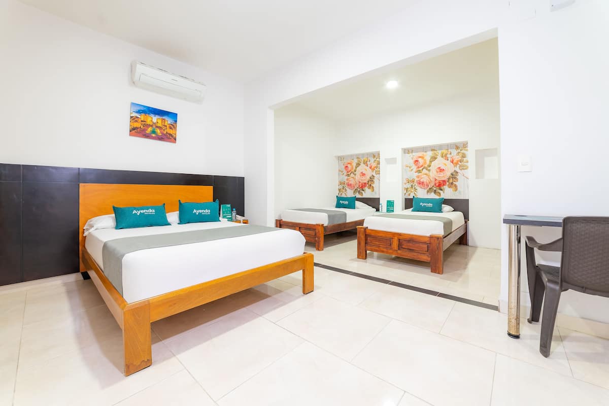 Quarto de hotel com uma cama grande, duas camas menores, uma escrivaninha e uma cadeira.