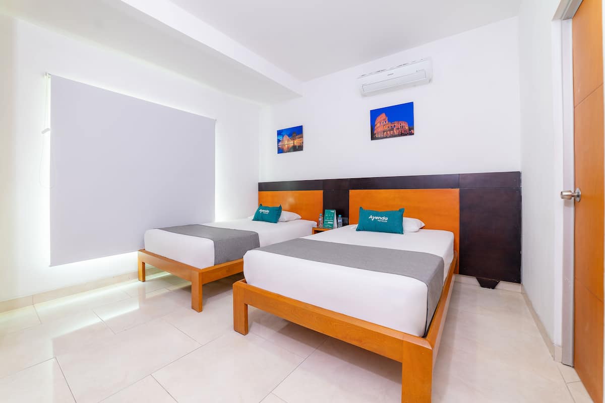 Quarto de hotel com duas camas, uma janela grande e dois aparelhos de ar condicionado fixados na parede.