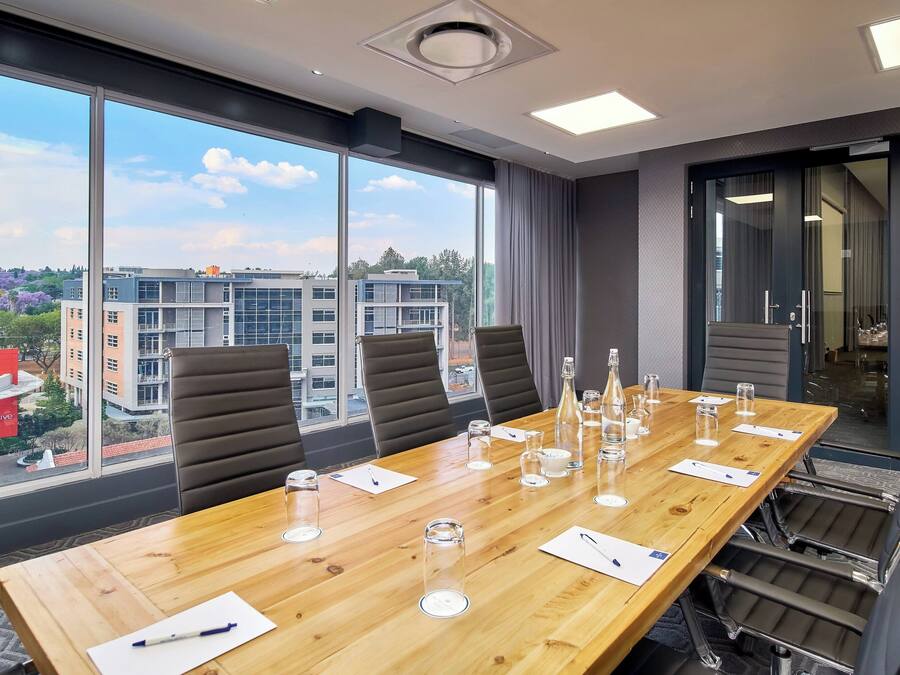 Uma sala de conferências com uma mesa grande, cadeiras e vista para edifícios através de amplas janelas.