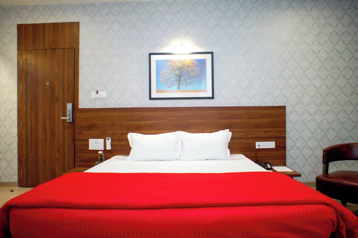 Quarto de hotel com cabeceira de madeira, colcha vermelha, quadro emoldurado na parede e guarda-roupa de madeira.