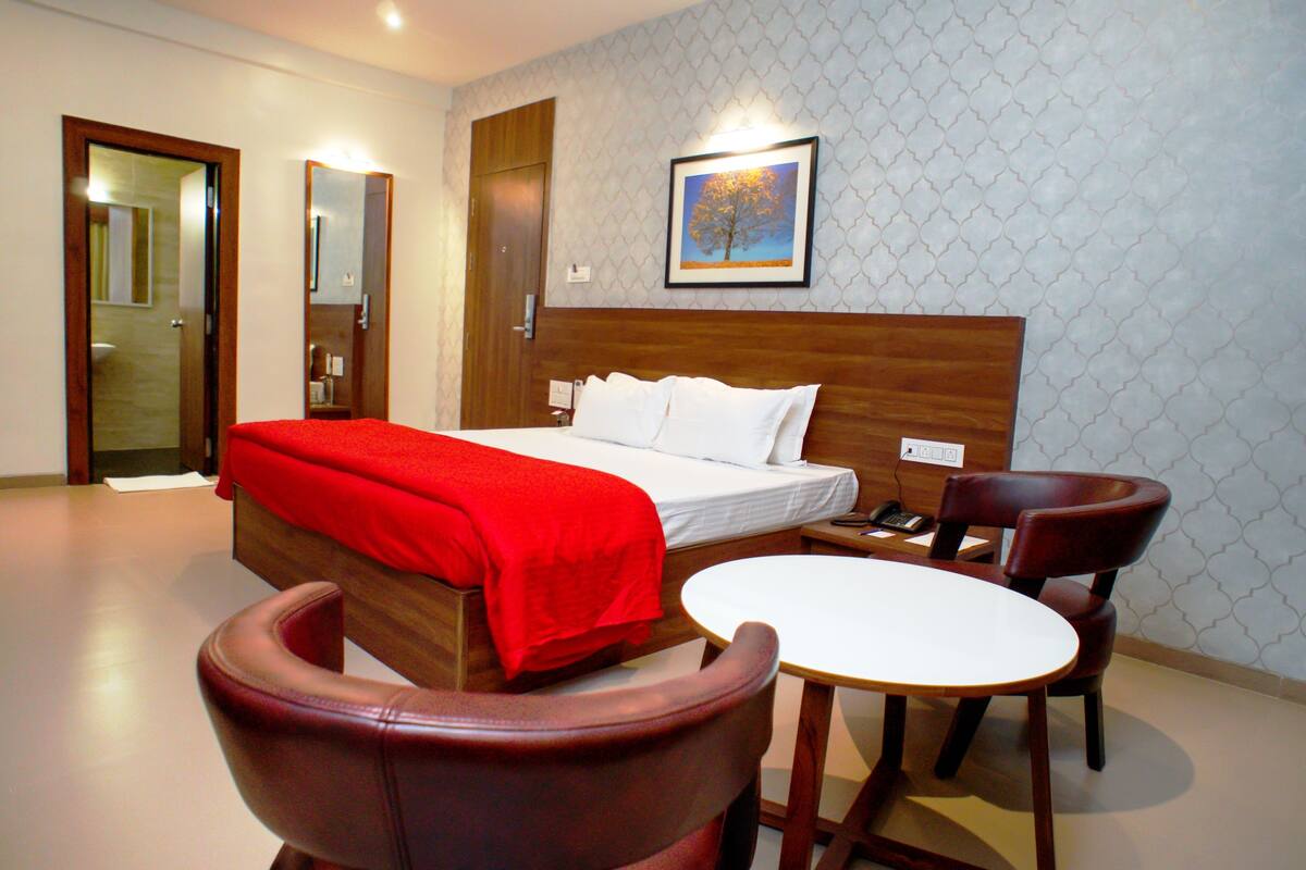 Quarto de hotel com uma cama, mesa de cabeceira com telefone, uma cadeira e uma pequena mesa.