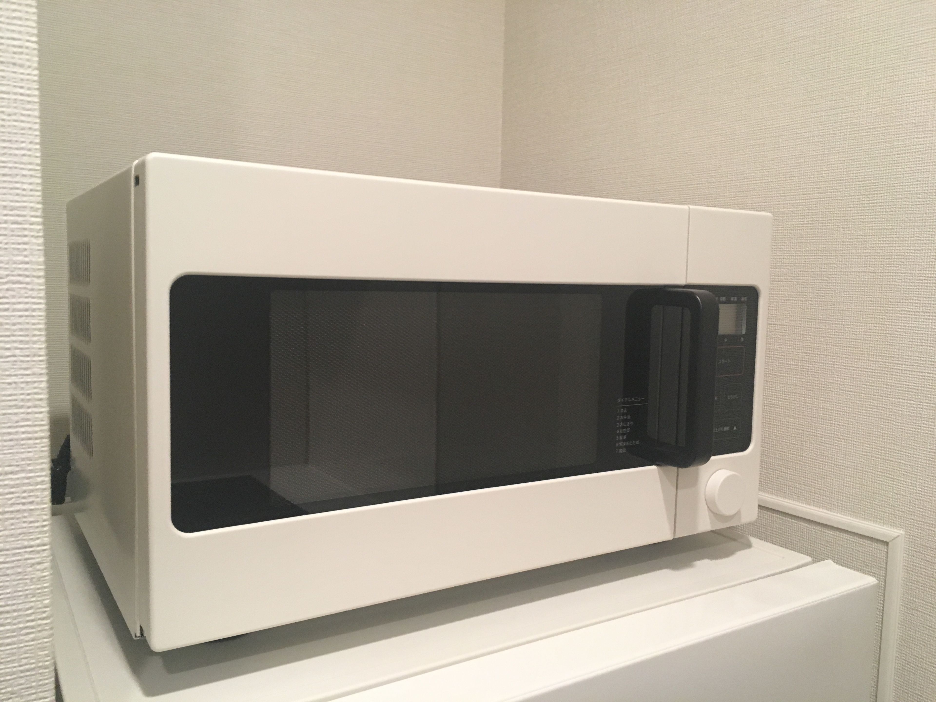 Um forno de micro-ondas branco com visor digital e painel de controle, sobre uma bancada branca.