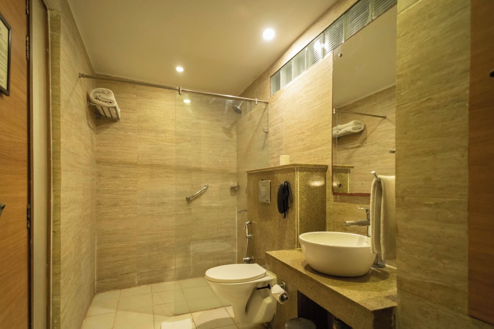 Um banheiro moderno com box de vidro, vaso sanitário, pia com espelho e porta-toalhas.