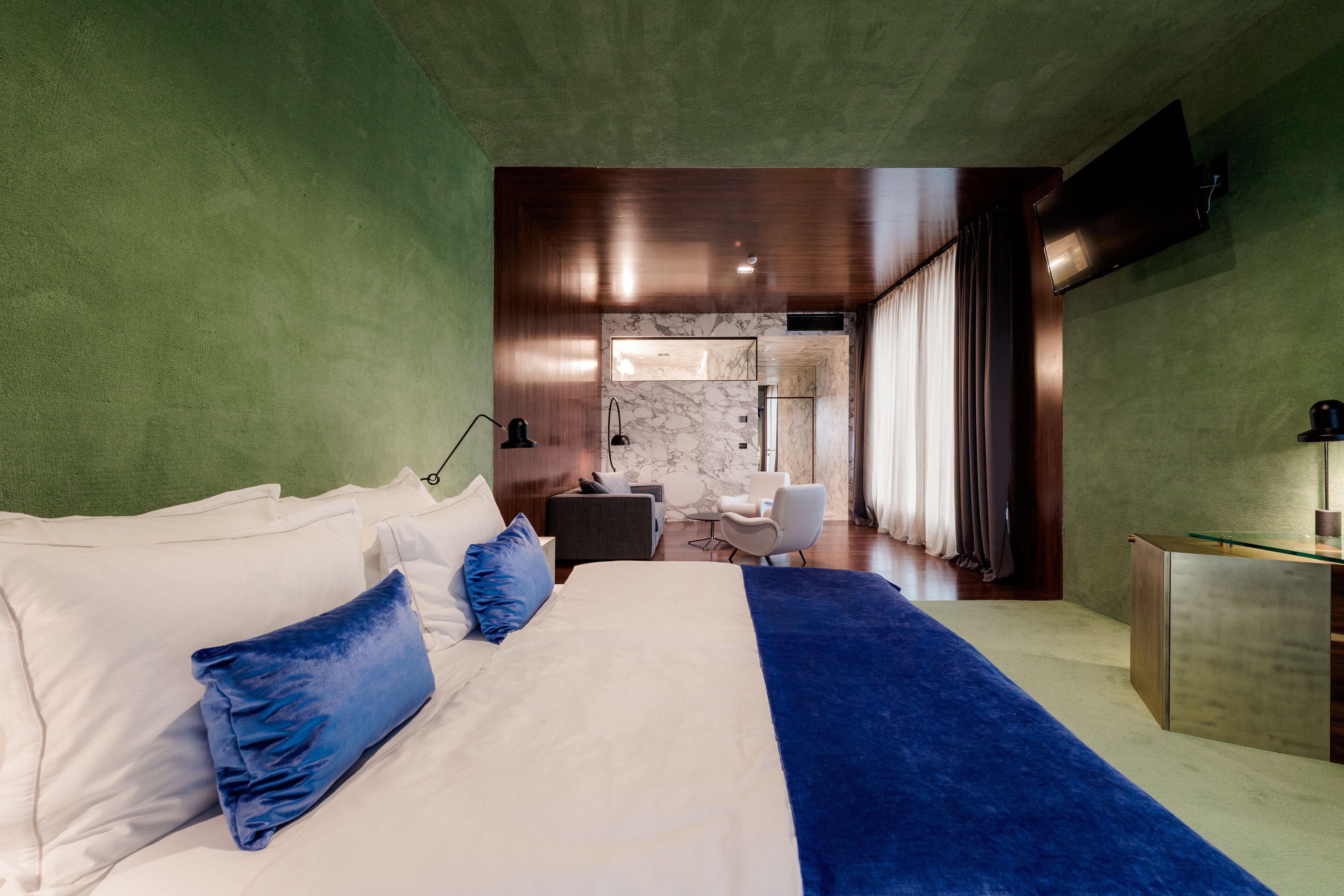 Quarto de hotel moderno com uma cama grande, uma mesa de trabalho e uma TV fixada na parede.