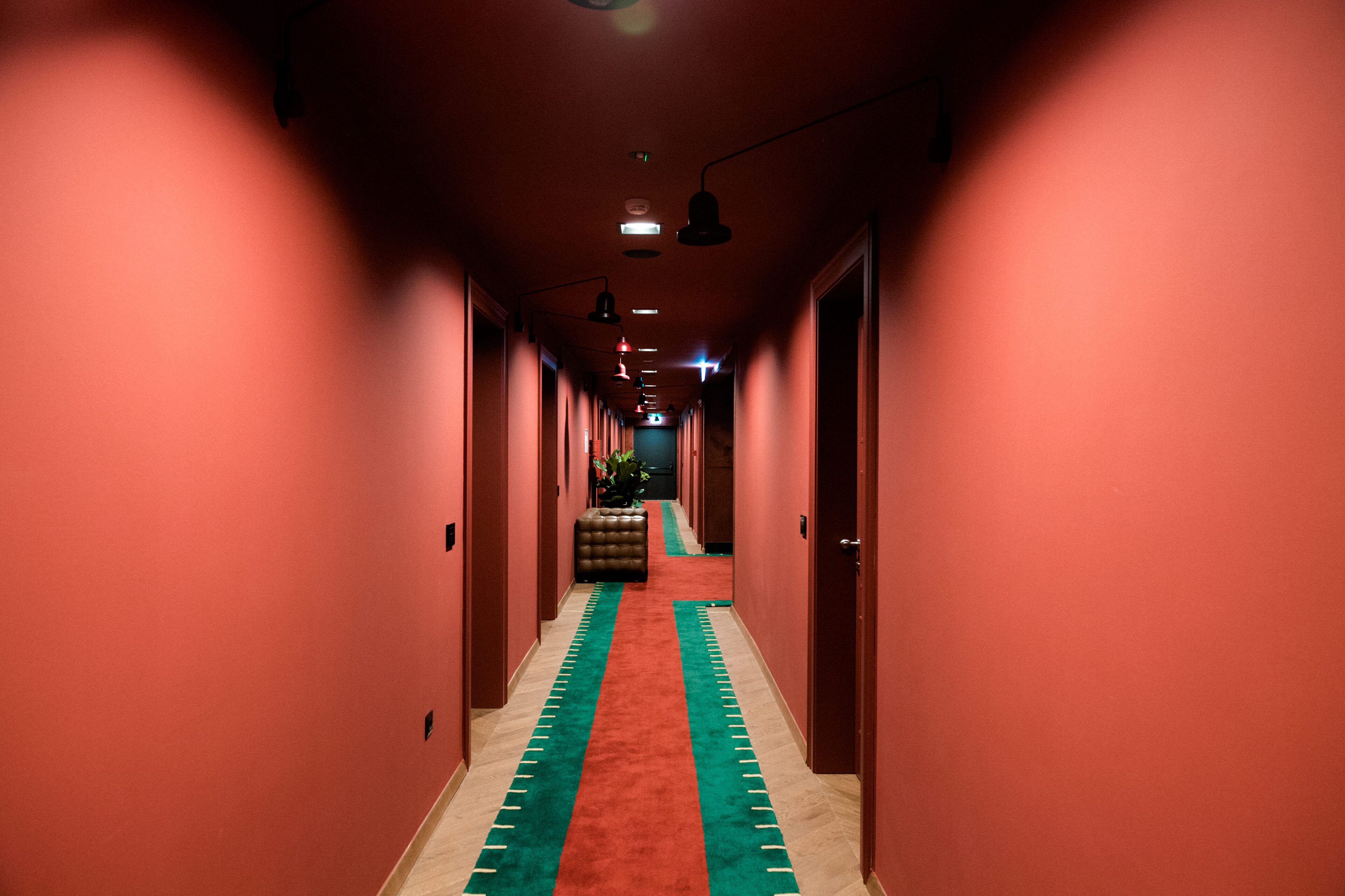 Corredor com paredes vermelhas, um tapete vermelho e um tapete verde que leva a um quarto.