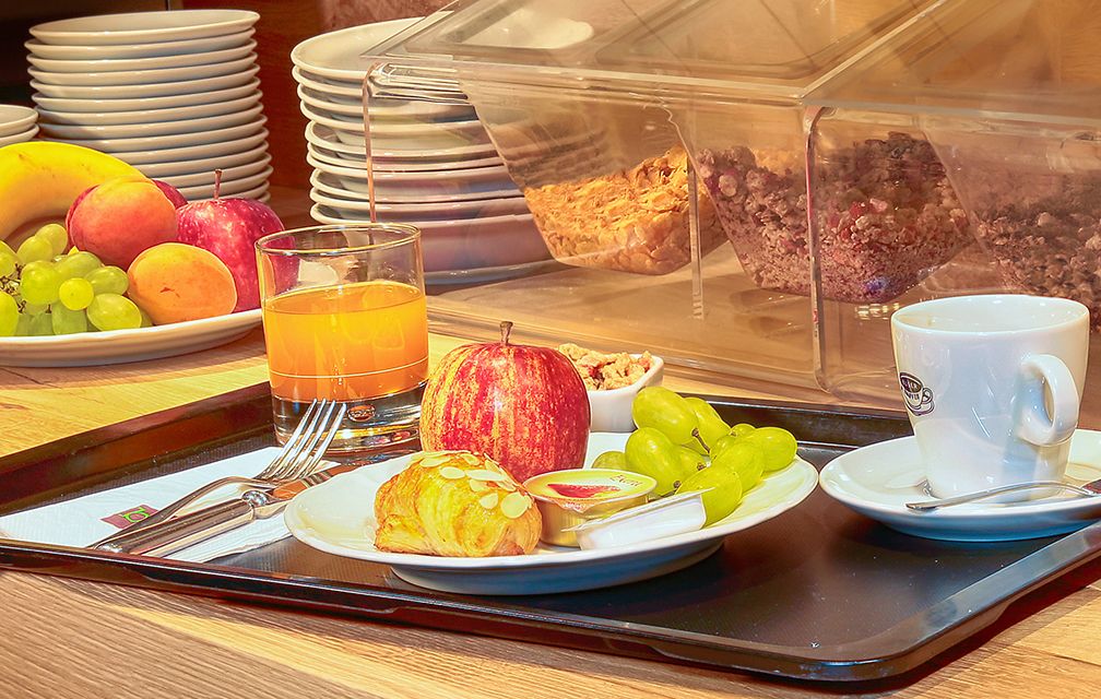 Bandeja de café da manhã com frutas, um copo de suco de laranja, um croissant e uma xícara de café.