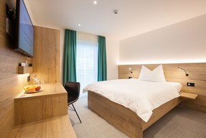 Quarto de hotel moderno com cama de madeira, escrivaninha com cadeira, televisão de tela plana e uma grande janela com cortinas.