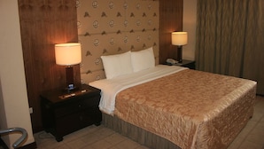 Quarto de hotel com cama, duas mesas de cabeceira, uma luminária em cada mesa, cabeceira estampada e cortina.
