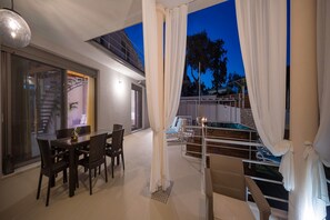 Uma área de jantar moderna com uma mesa e cadeiras, uma escada e uma piscina visível através das cortinas.