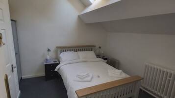 Quarto com claraboia, cama, mesa de cabeceira e radiador.