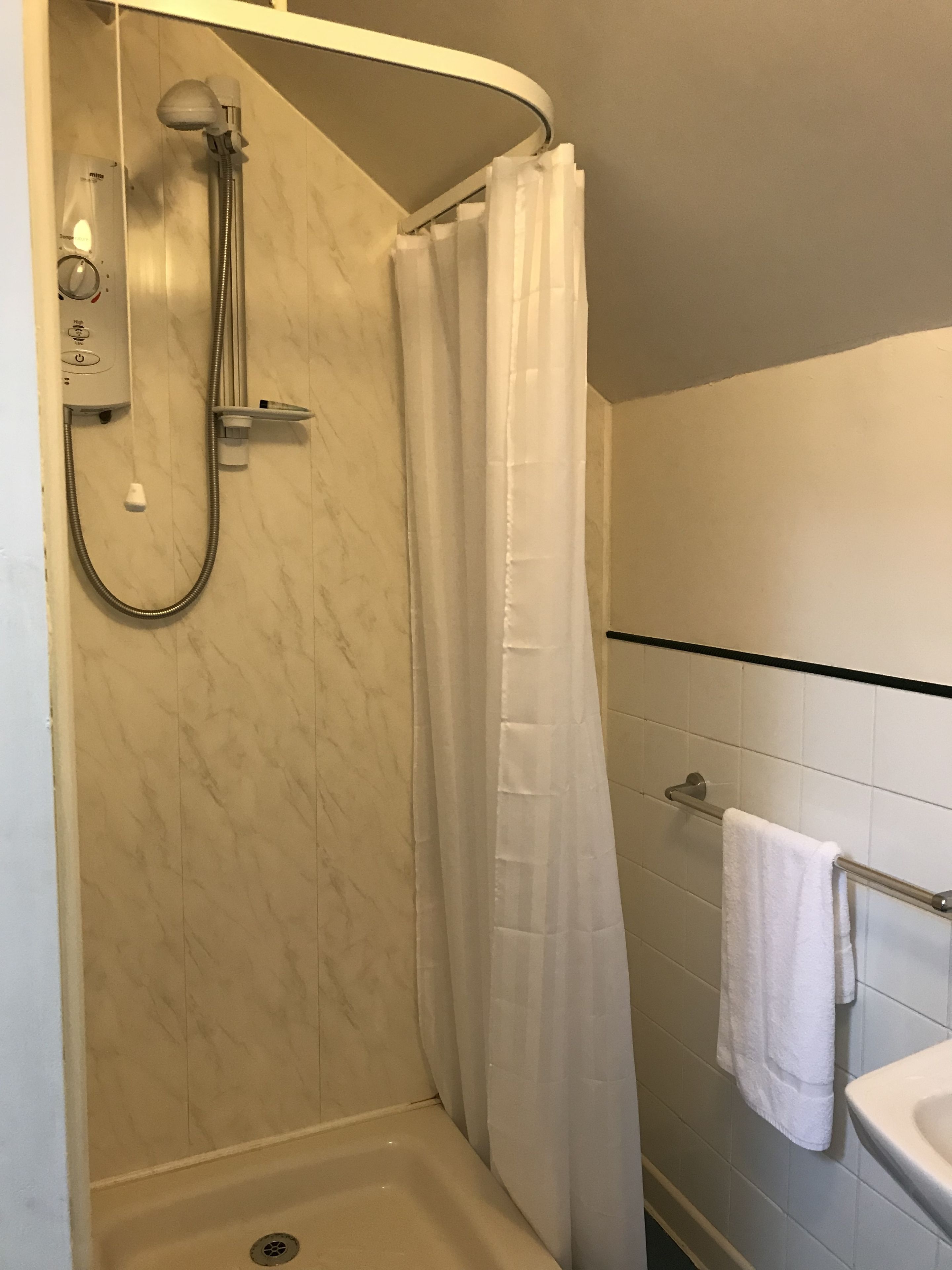 Um chuveiro com chuveiro manual, box de vidro e cortina branca.