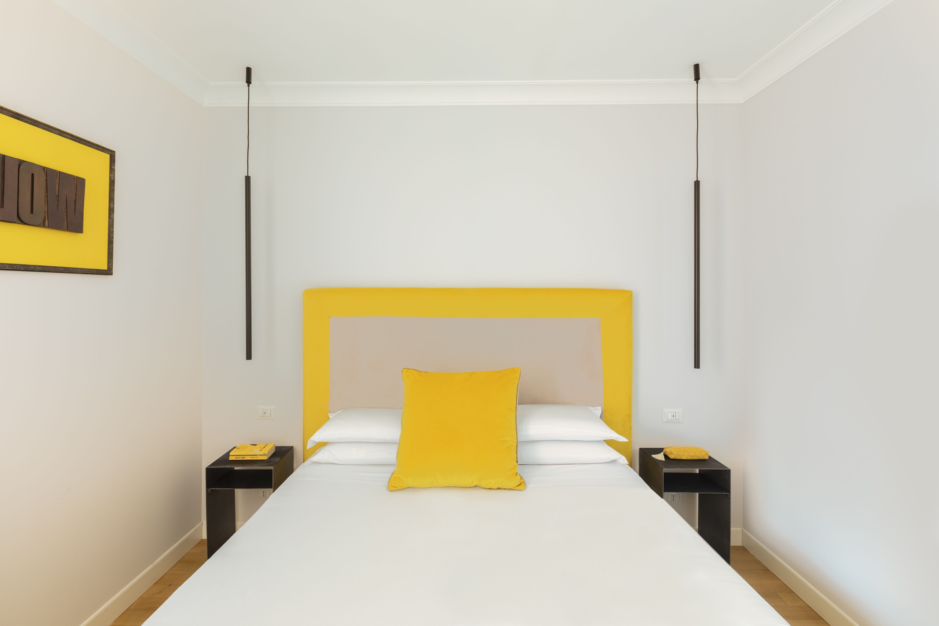 Quarto de hotel moderno, com uma cama centralizada, acompanhada por duas mesas de cabeceira.