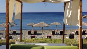 Um espaço de relaxamento à beira-mar com pérgulas de madeira e guarda-sóis de palha, com vista para o mar.