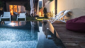 Uma piscina com água cristalina, rodeada por um deck de madeira e espreguiçadeiras brancas.