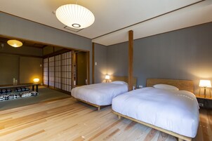 Quarto de hotel com duas camas, piso de madeira e portas deslizantes tradicionais japonesas.