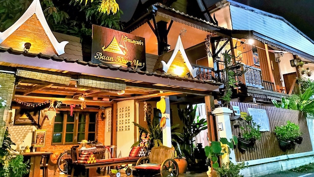 Um restaurante tailandês tradicional com área de estar coberta ao ar livre, uma placa e um alpendre decorativo.