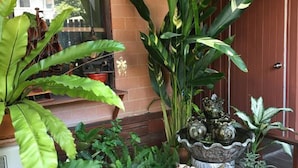 Varanda com vasos de plantas, uma pequena estátua e um banco de madeira.