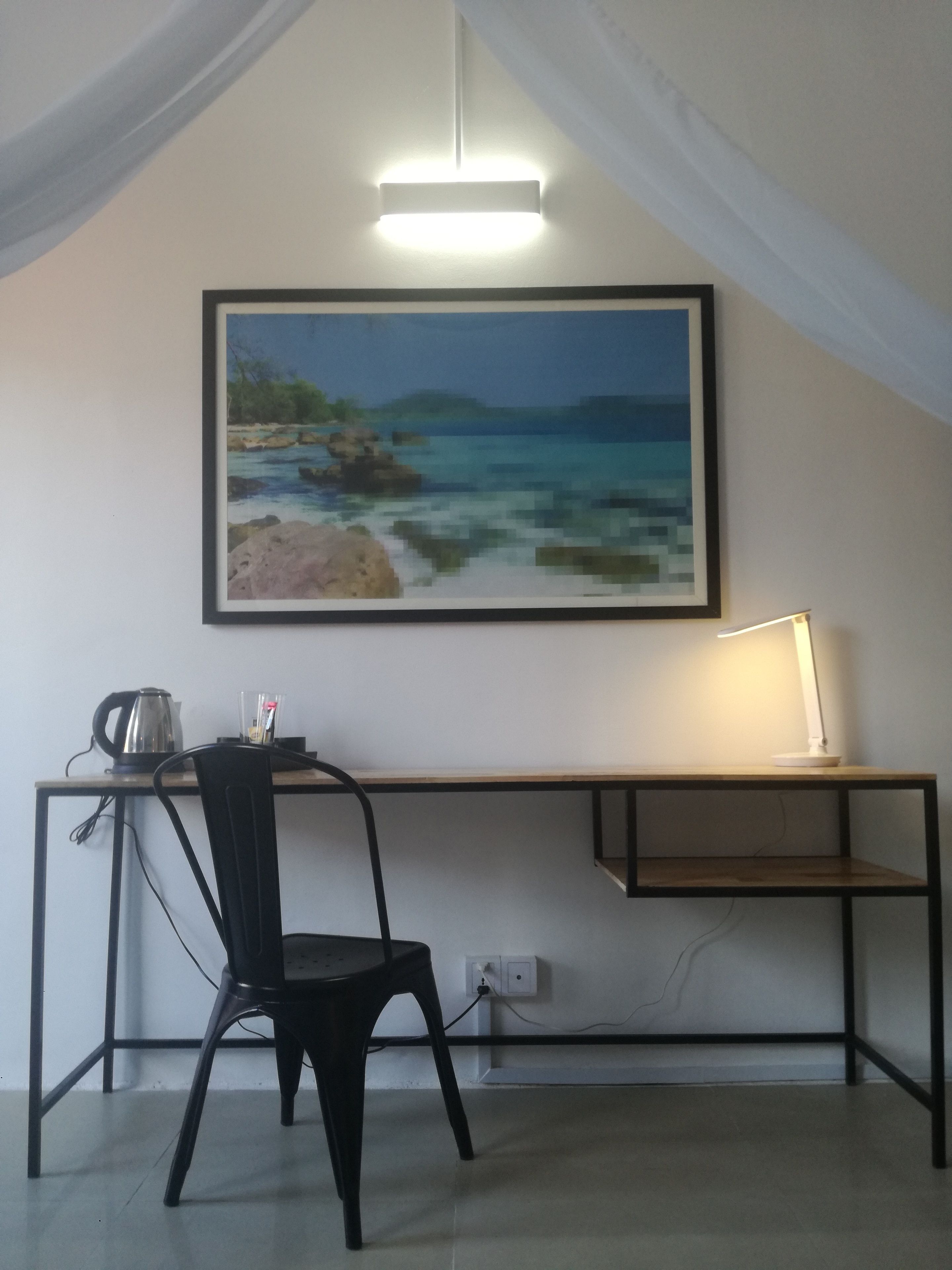 Quarto com escrivaninha, cadeira e um quadro de uma praia.