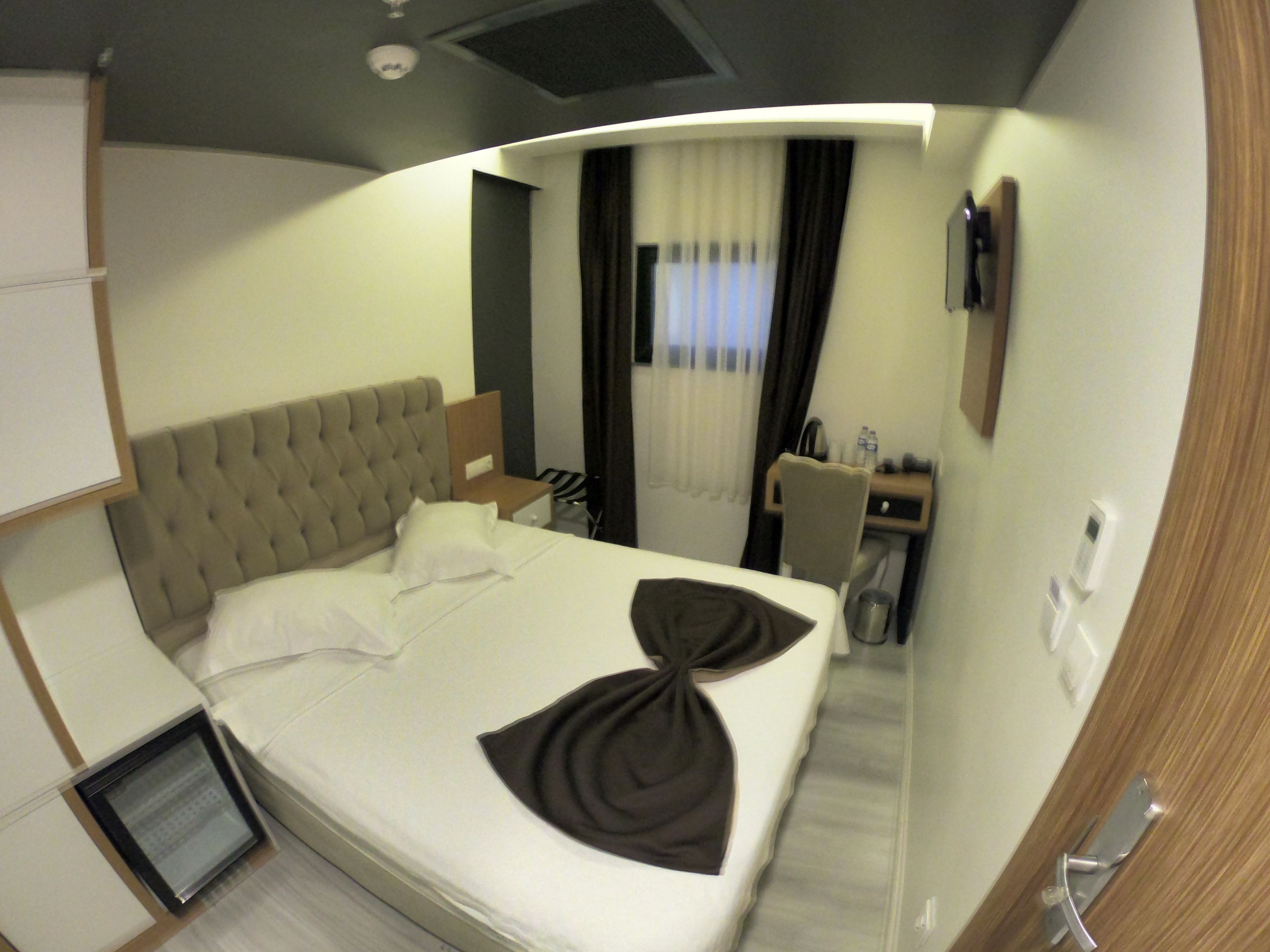 Quarto de hotel com cama grande, escrivaninha, cadeira, mesa pequena, espelho e janela com cortinas.