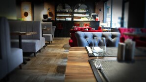 Um restaurante com chão de madeira, assentos cinzas e vermelhos, e um bar ao fundo.