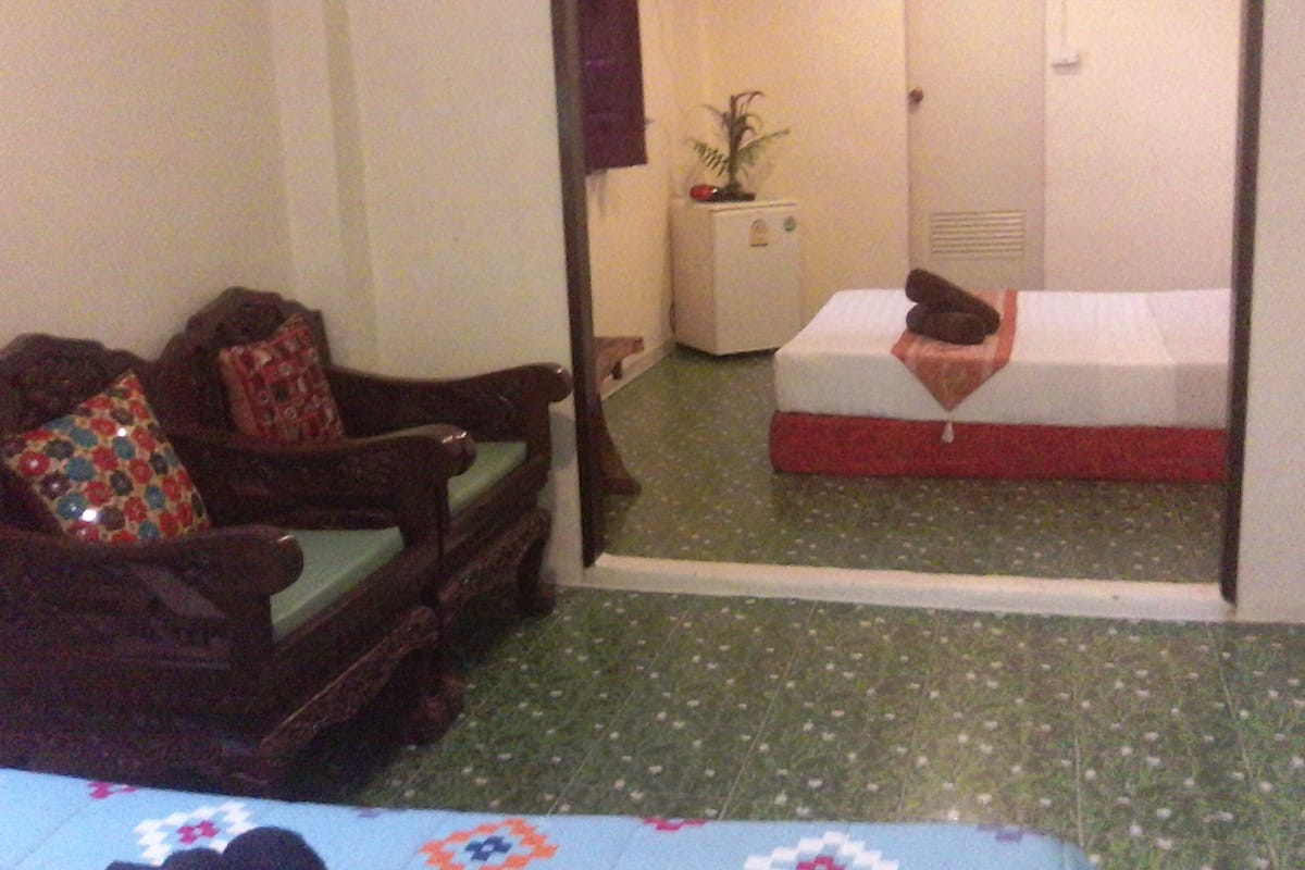 Quarto de hotel com uma cama, mesa de cabeceira, uma cadeira e uma planta em vaso.