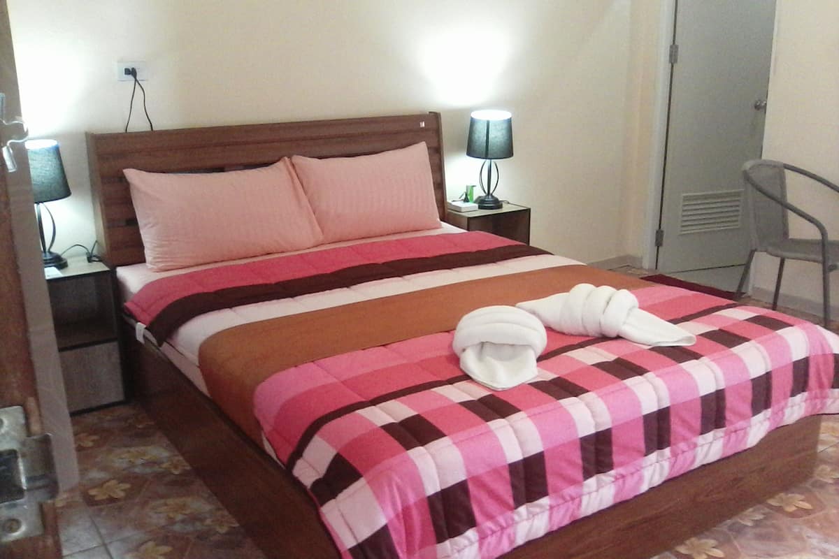 Uma cama bem arrumada com roupa de cama rosa e marrom, uma toalha dobrada e um abajur em uma mesa de cabeceira.