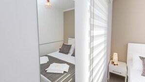 Quarto de hotel com cama, mesa de cabeceira, abajur e espelho refletindo o ambiente.