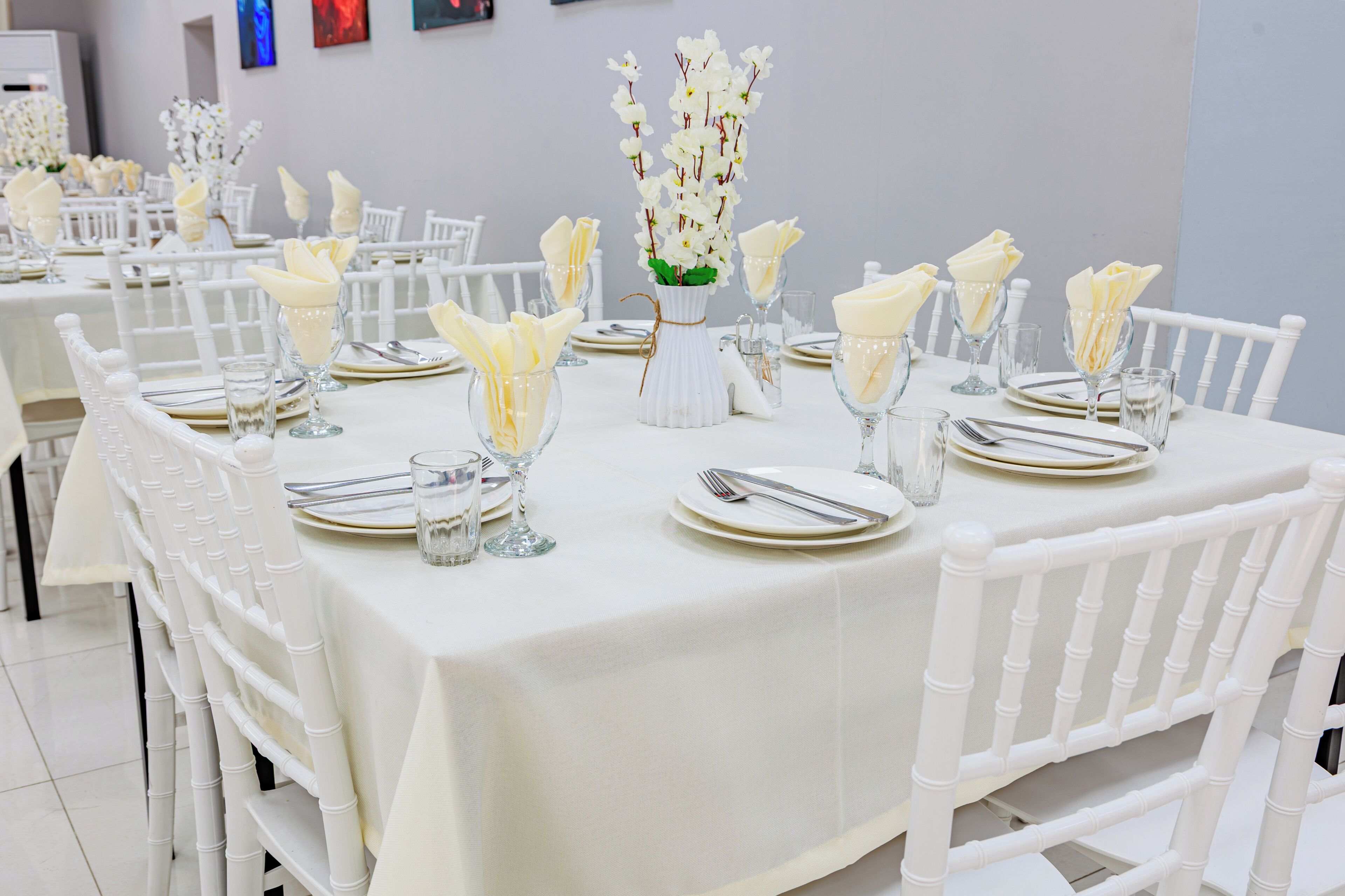 Uma sala de jantar com toalhas de mesa brancas, mesas bem arrumadas com copos, pratos e guardanapos dobrados.