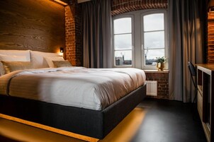 Quarto moderno com uma cama grande, parede de tijolos decorativa, janela com cortinas e vista para a cidade.