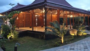 Um edifício de estilo tradicional com telhado de telhas e estrutura de madeira, rodeado por um jardim bem cuidado com palmeiras.
