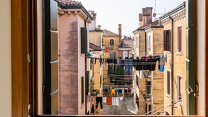 Rua estreita com edifícios em ambos os lados, varal com roupa e um batente de porta visível.